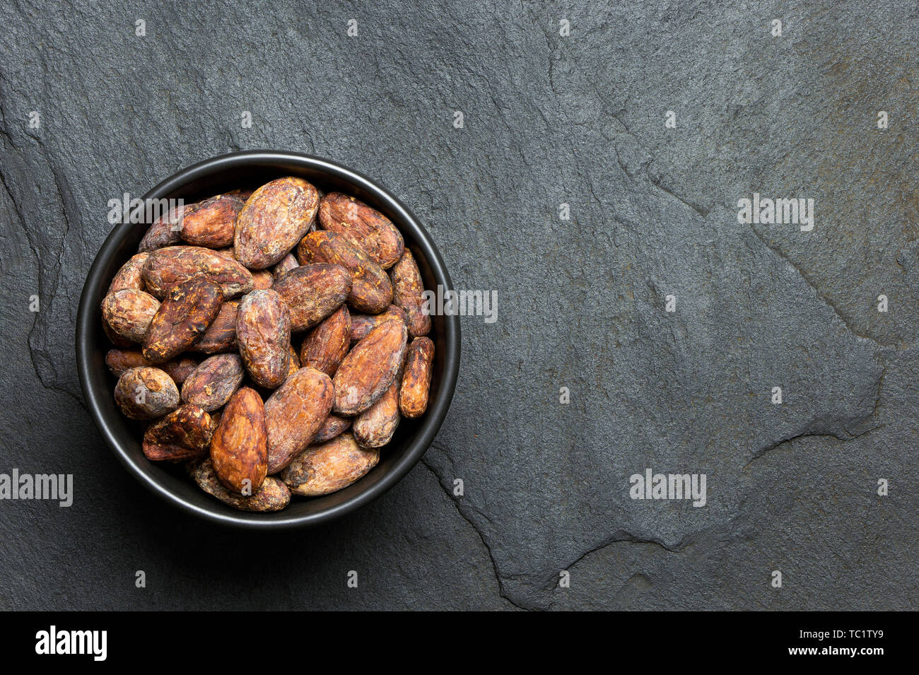Roasted unpeeled cocoa beans in a black ceramic bowl isolated on black ...