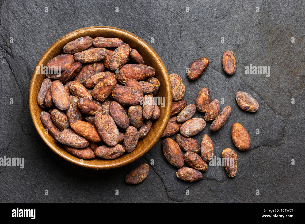 Roasted unpeeled cocoa beans in a brown wooden bowl next to unpeeled ...