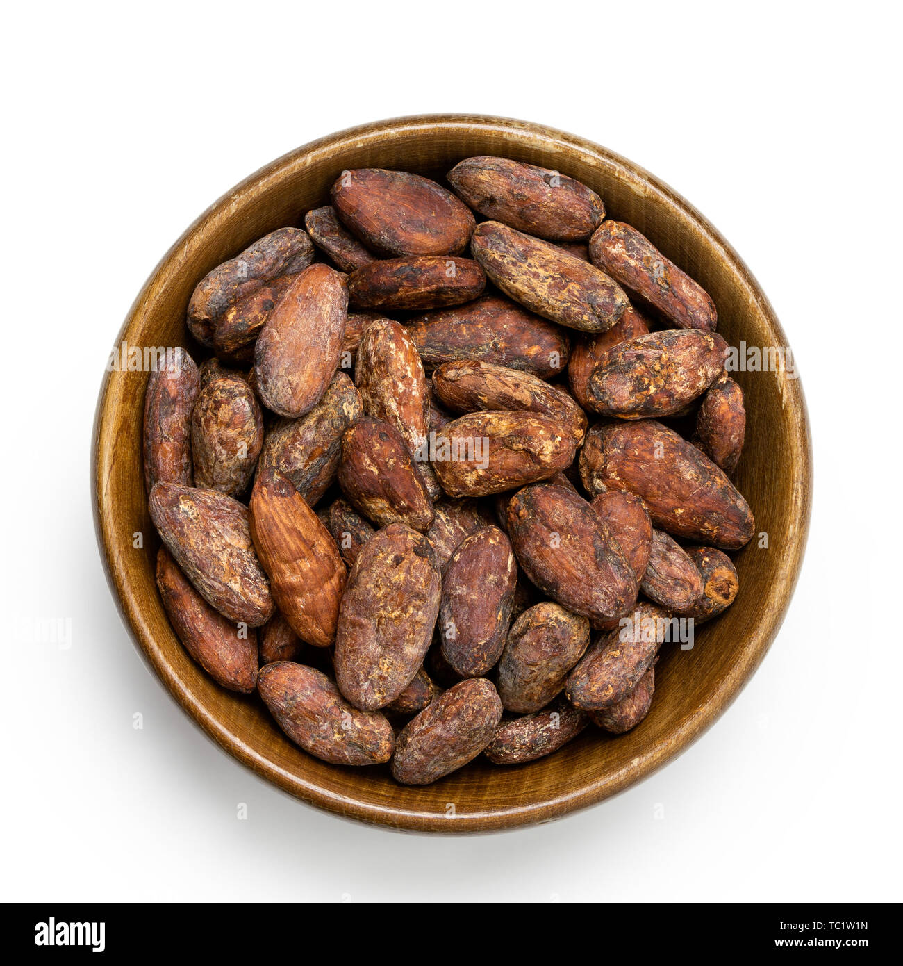 Roasted unpeeled cocoa beans in a brown wooden bowl isolated on white ...