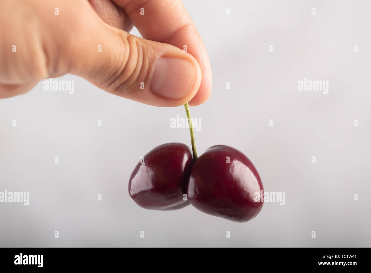 Man holds two ugly cherries with his fingers. Strange shape berries on ...