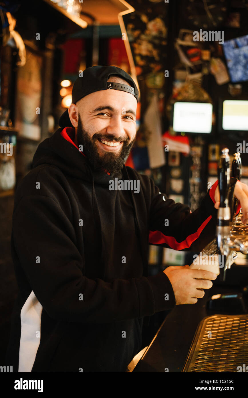 smiling barman pouring beer in a bar. Bearded courageous man pours you ...