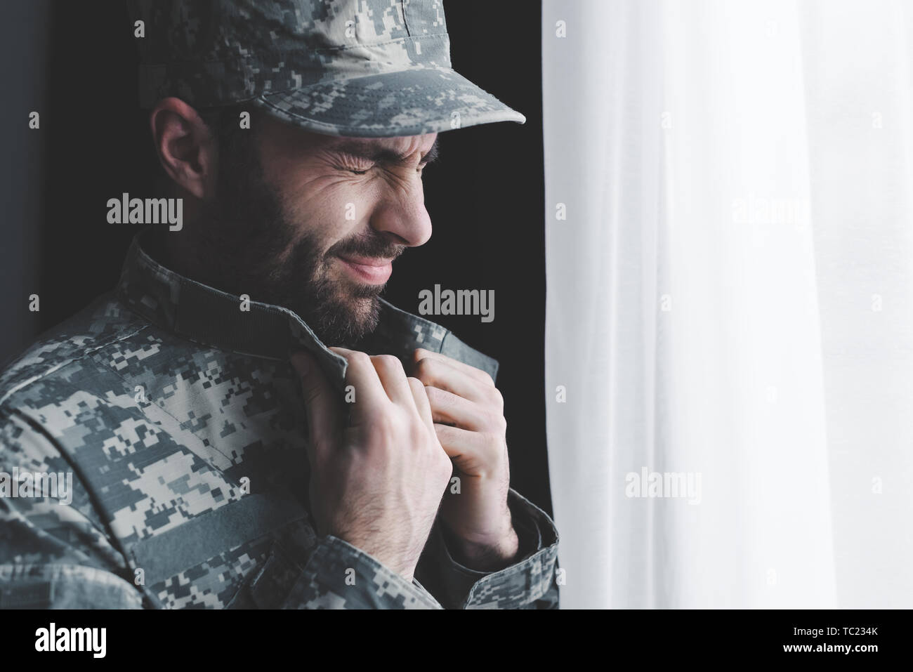 depressed bearded man in military uniform crying while standing by ...