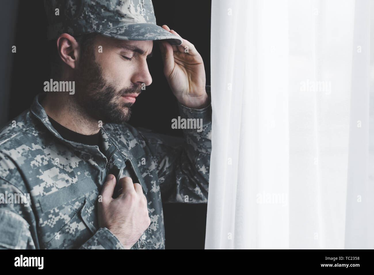 pensive bearded man in uniform holding hand on chest while standing by ...