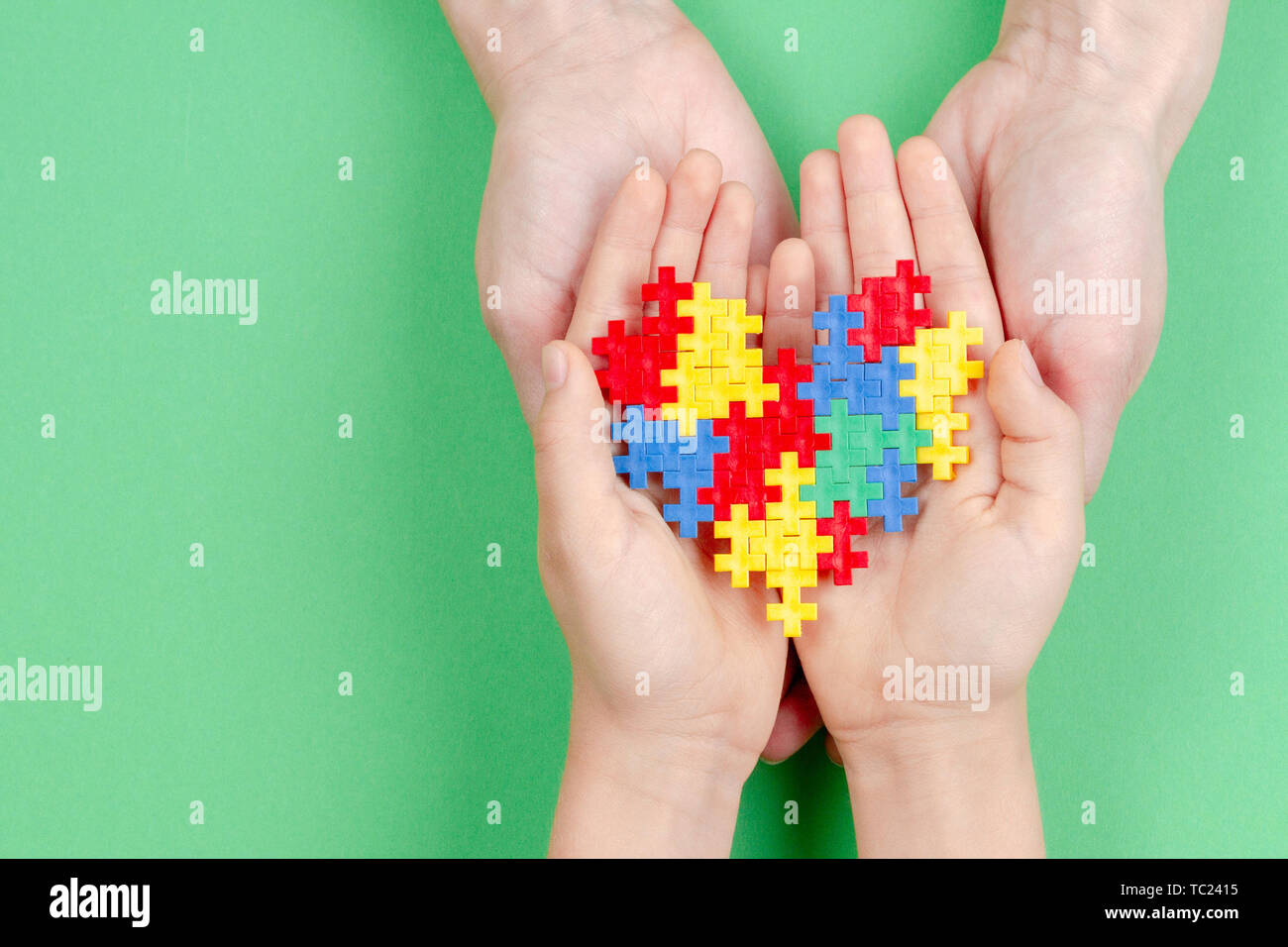 Adult and kid hands holding colorful heart on green background. World ...
