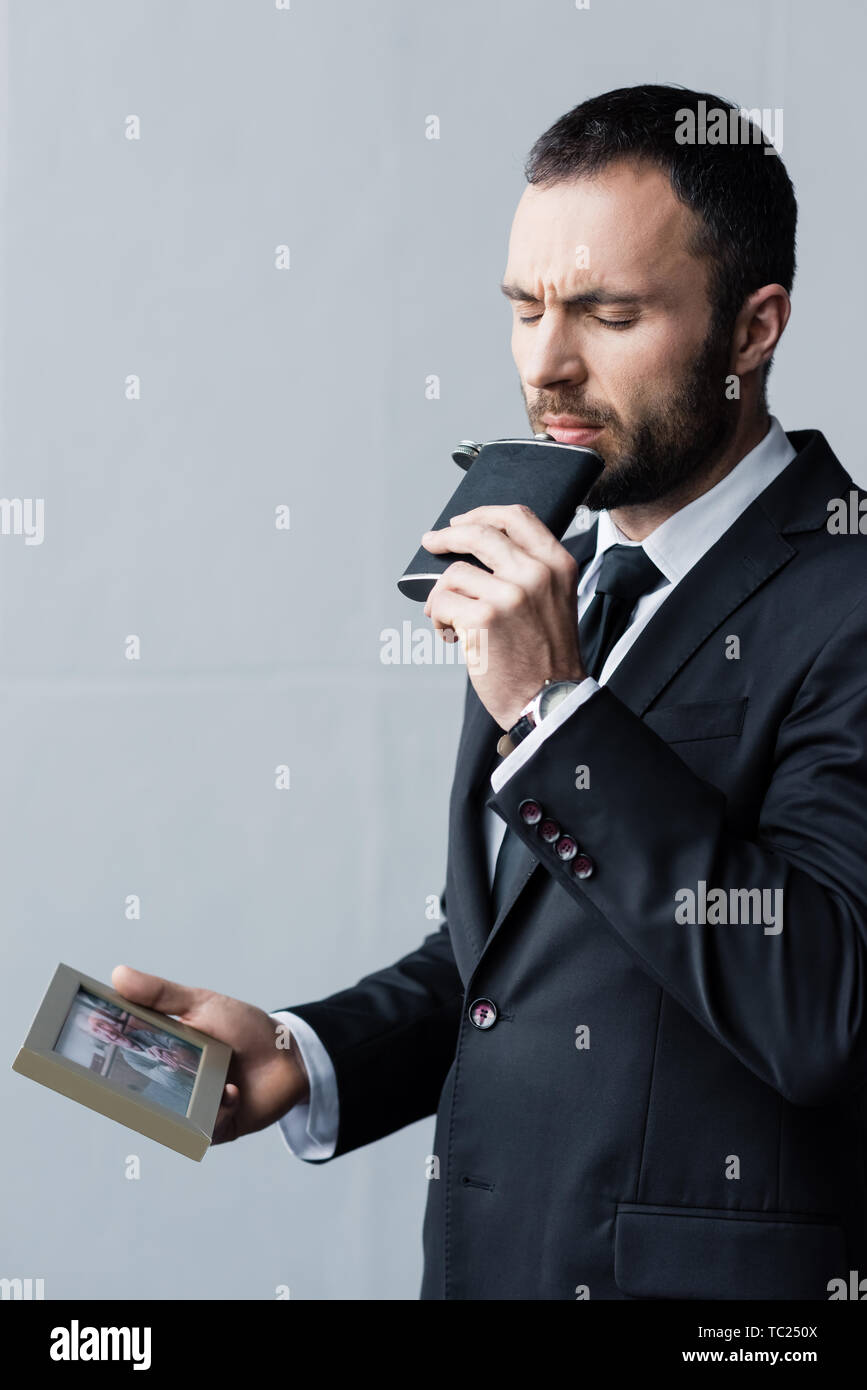 upset handsome man drinking from flask with closed eyes while holding ...