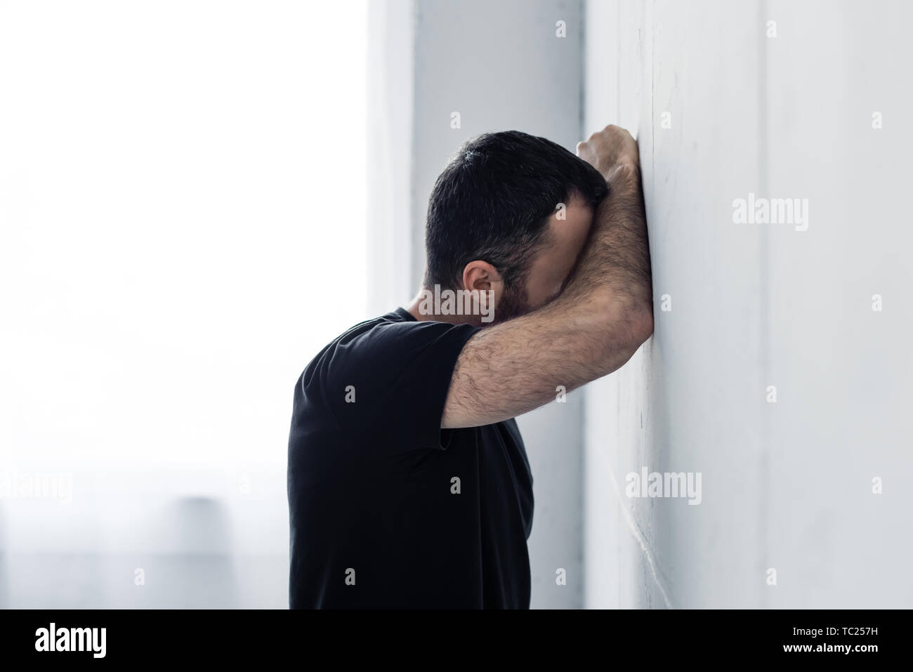 adult depressed man in black t-shirts standing near white wall at home ...