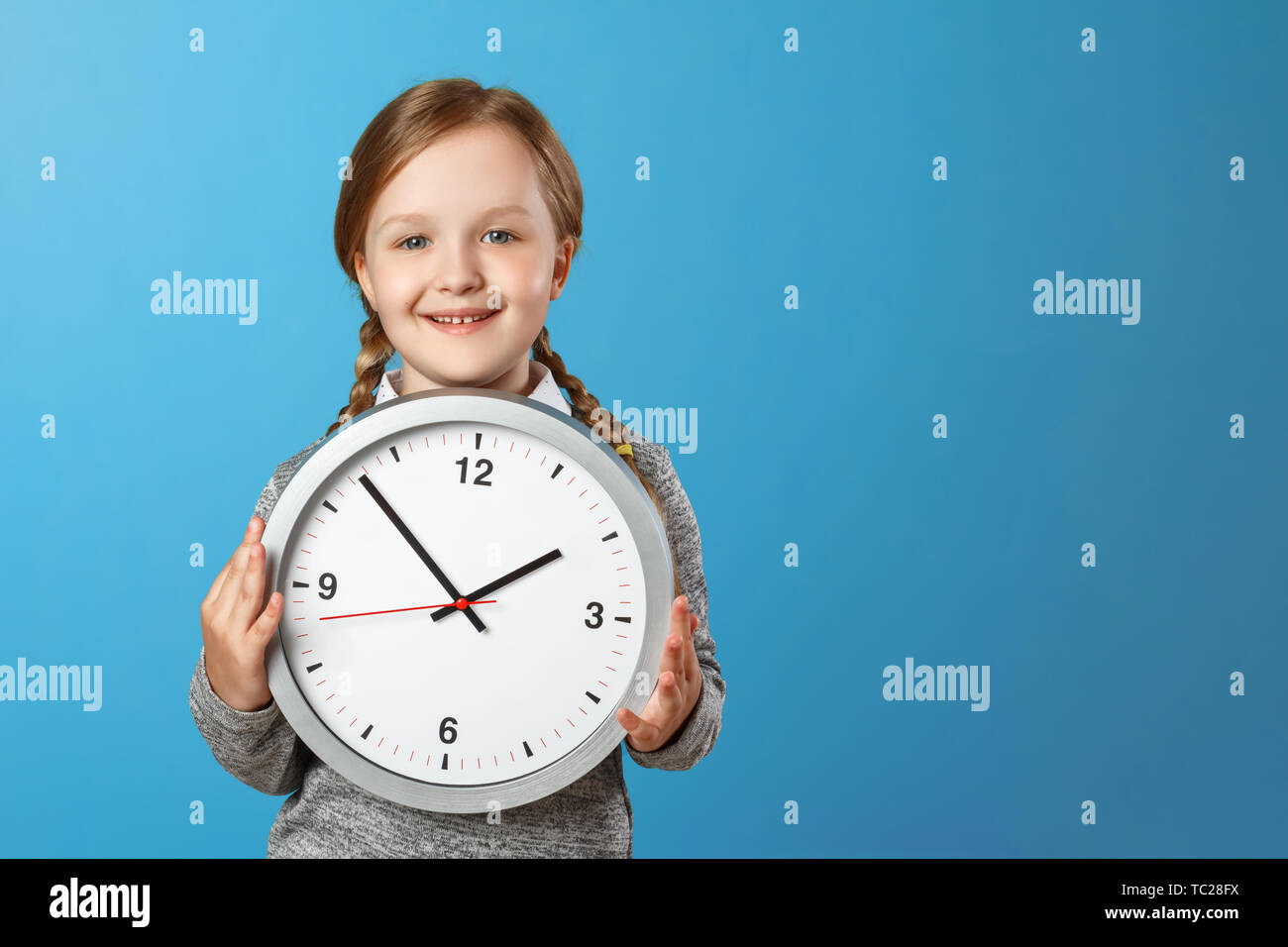 A cute little girl holding a big clock over a blue background. The ...