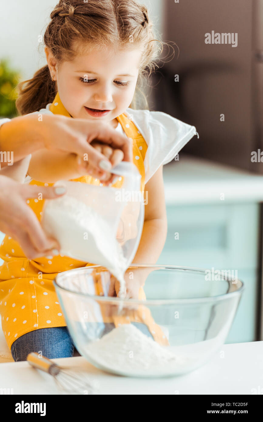 selective focus of woman adding flour to bowl near excited daughter in ...