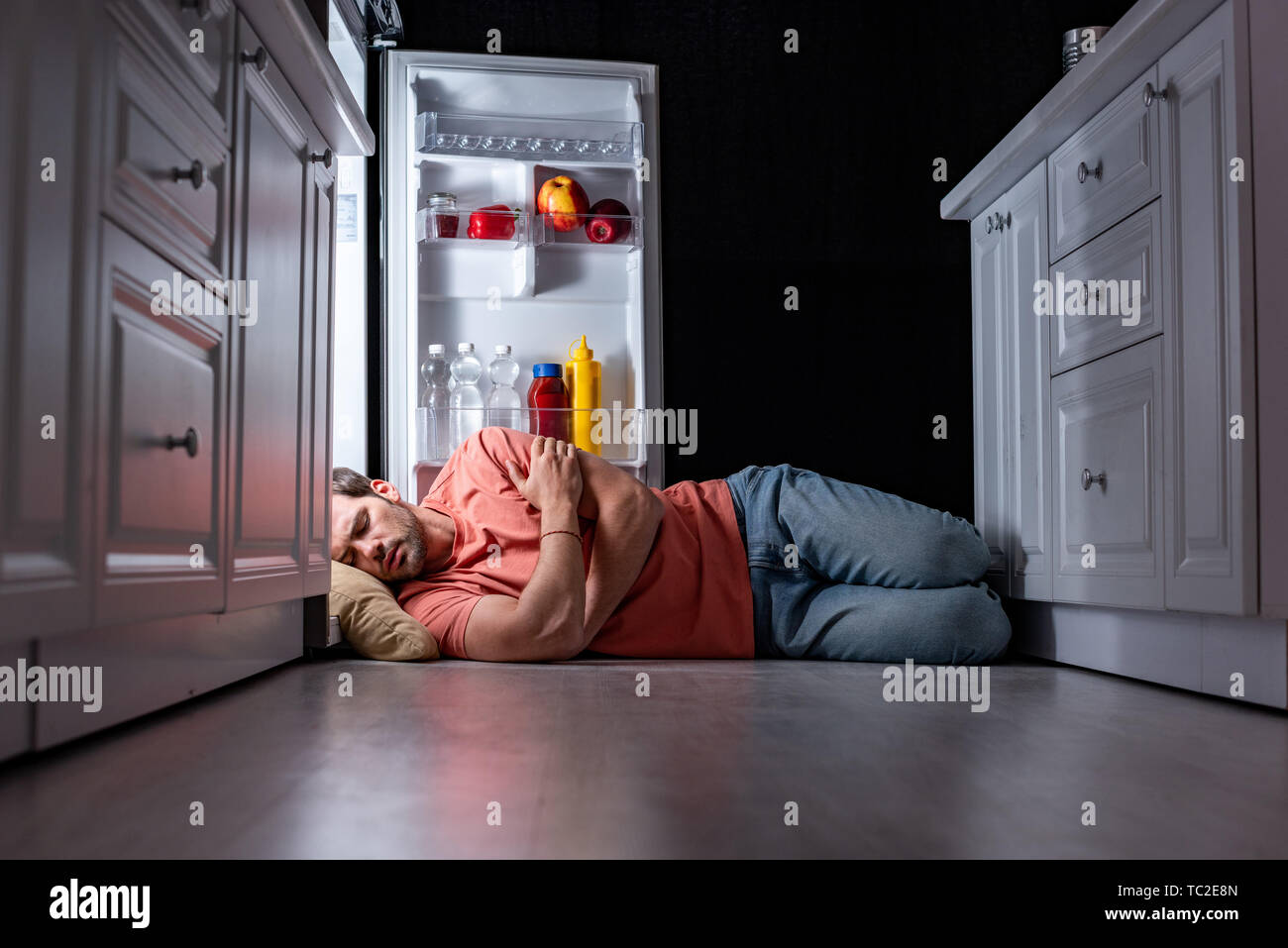 exhausted young man sleeping on kitchen floor near open refrigerator ...