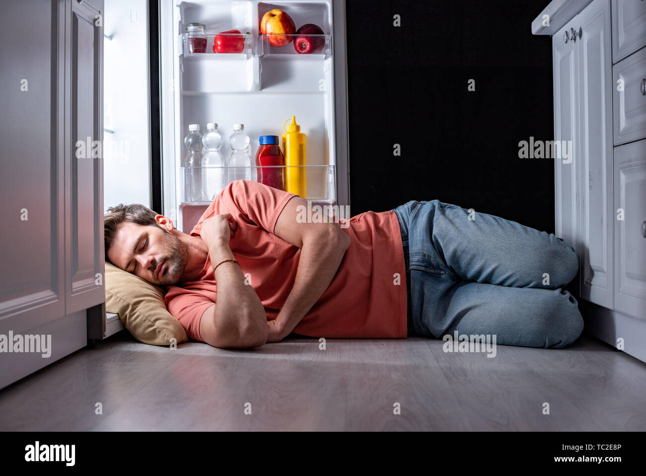 exhausted man sleeping on floor in kitchen near open refrigerator Stock ...