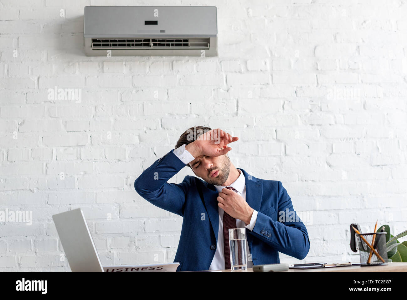 handsome businessman suffering from heat while sitting at workplace ...