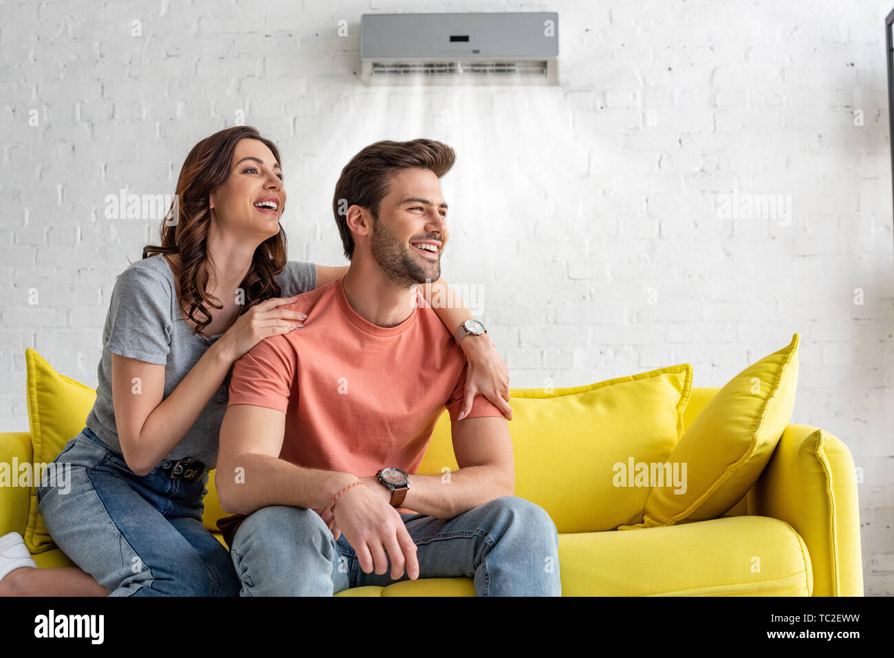 cheerful couple sitting on yellow sofa under air conditioner at home Stock Photo - Alamy