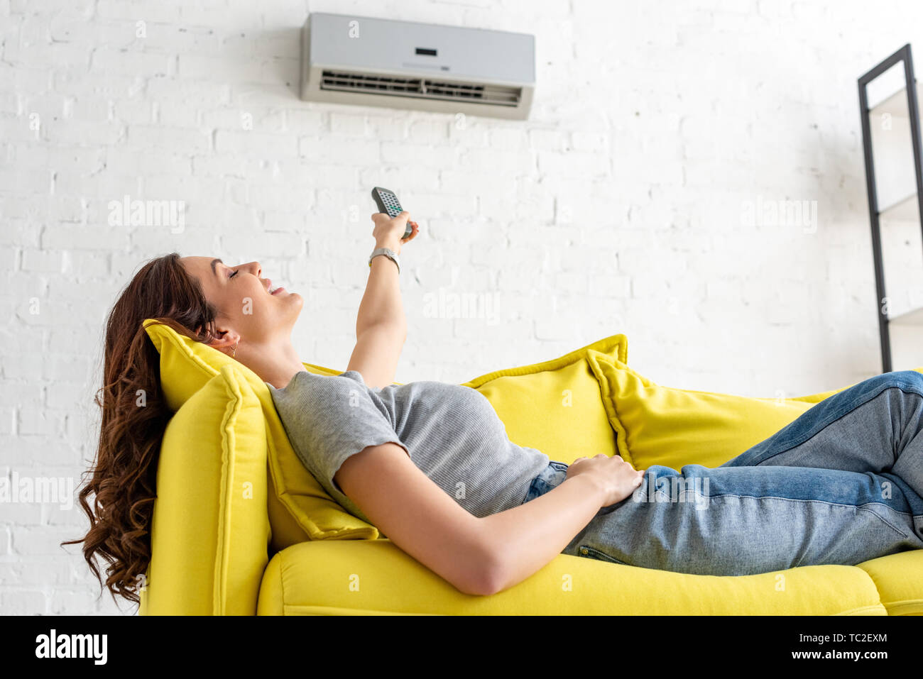 attractive young woman relaxing under air conditioner and holding ...