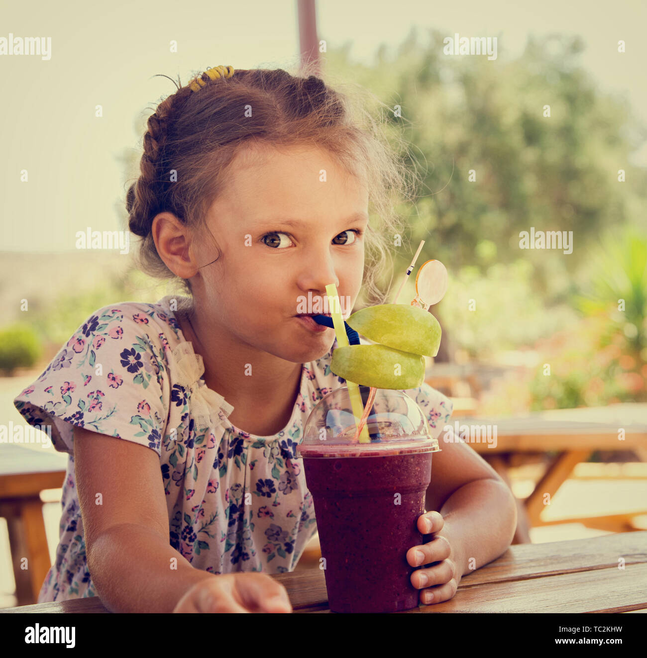 Cute smiling thinking kid girl drinking smoothie juice with fun look in ...