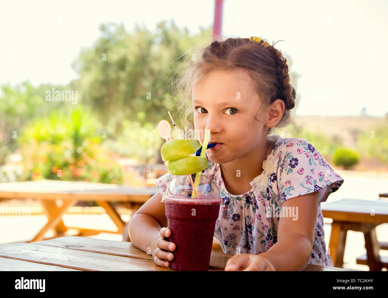 Cute smiling thinking kid girl drinking smoothie juice with fun look in ...