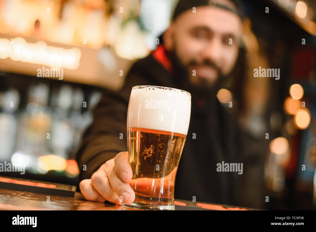 Bearded and smiling barman gives beer. Cool and courageous bar. A happy ...