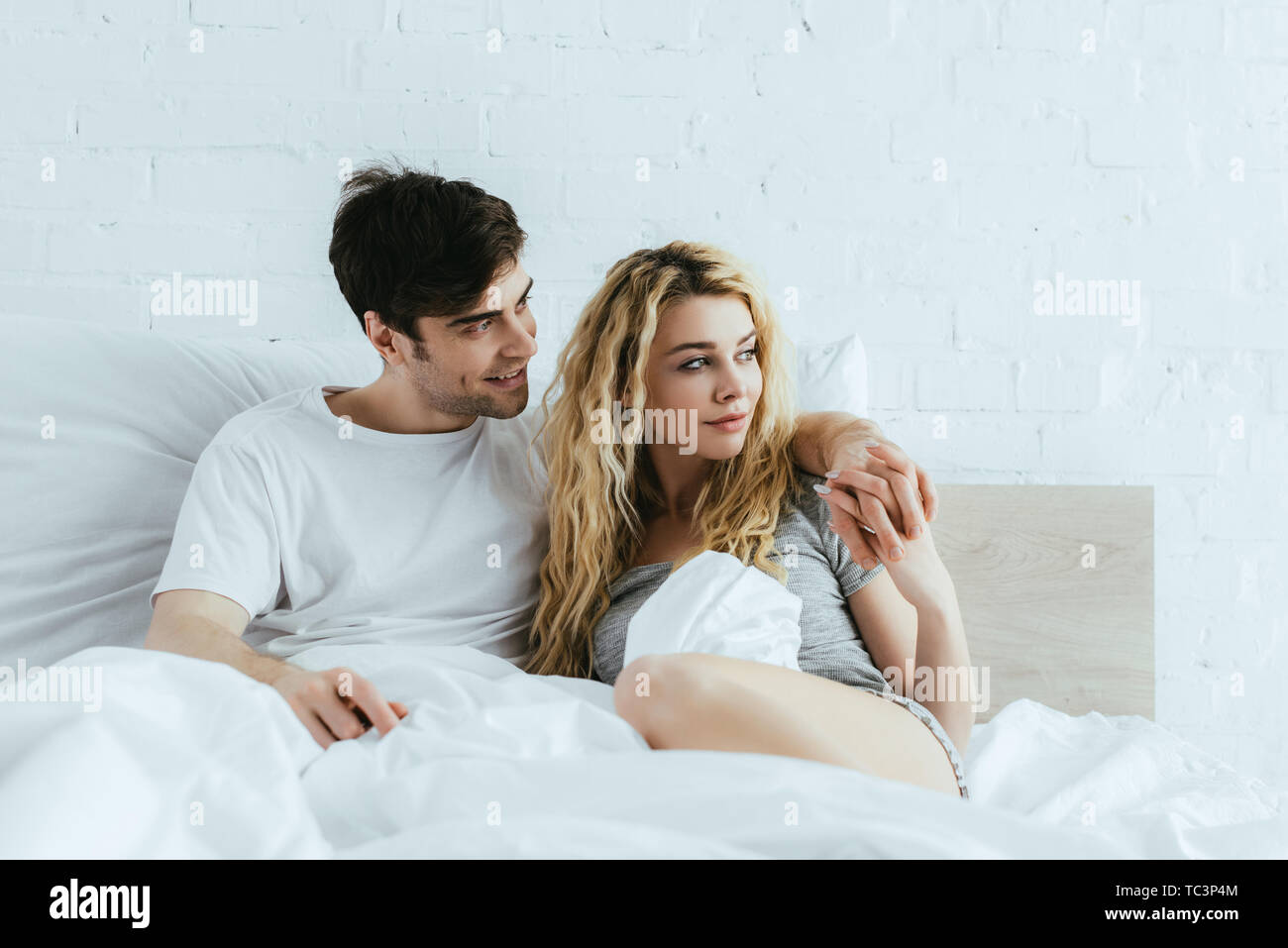 happy man holding hands with beautiful girlfriend while lying in bed ...