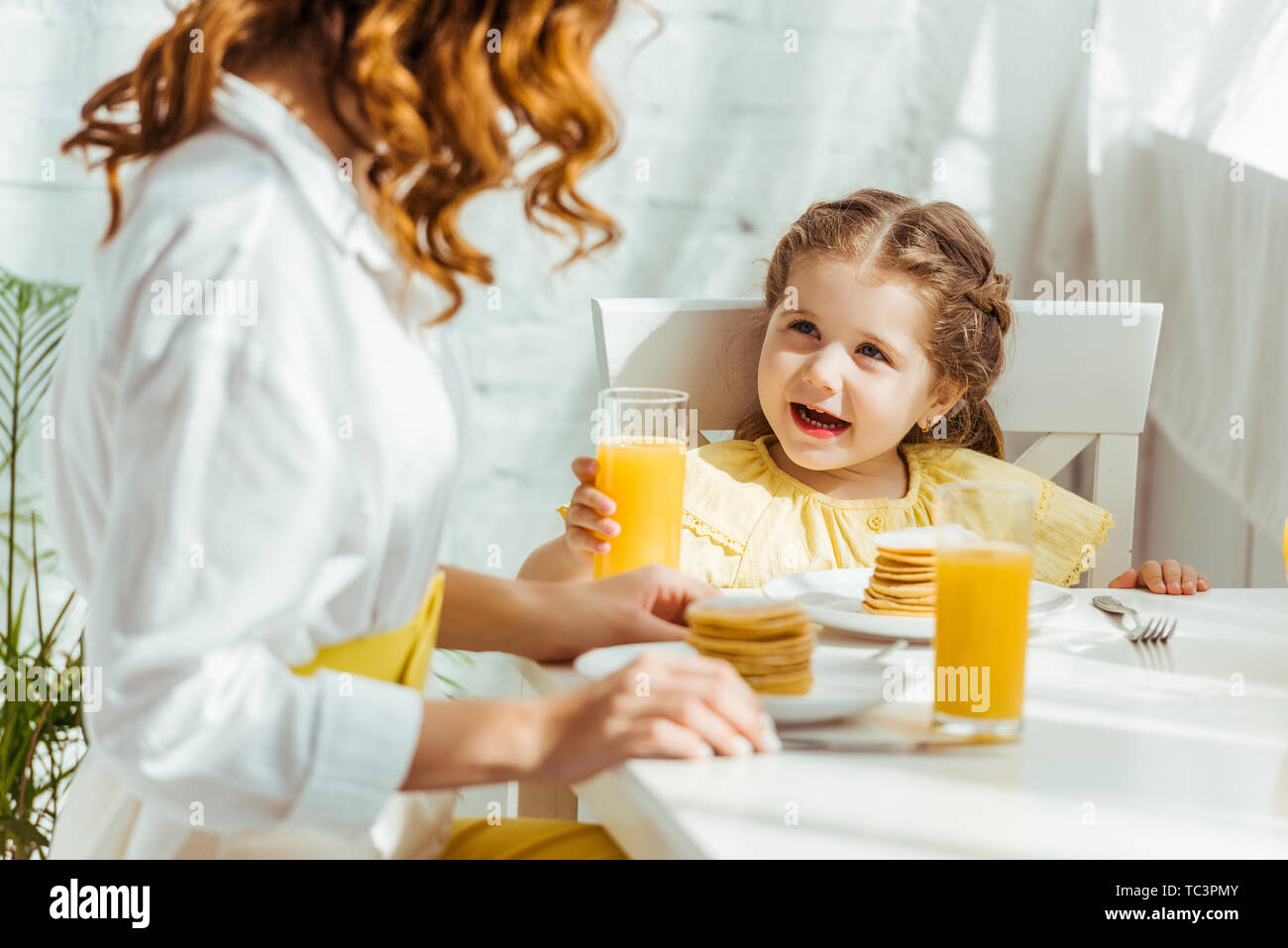 selective focus of cute happy child holding glass with orange juice while having breakfast with ...
