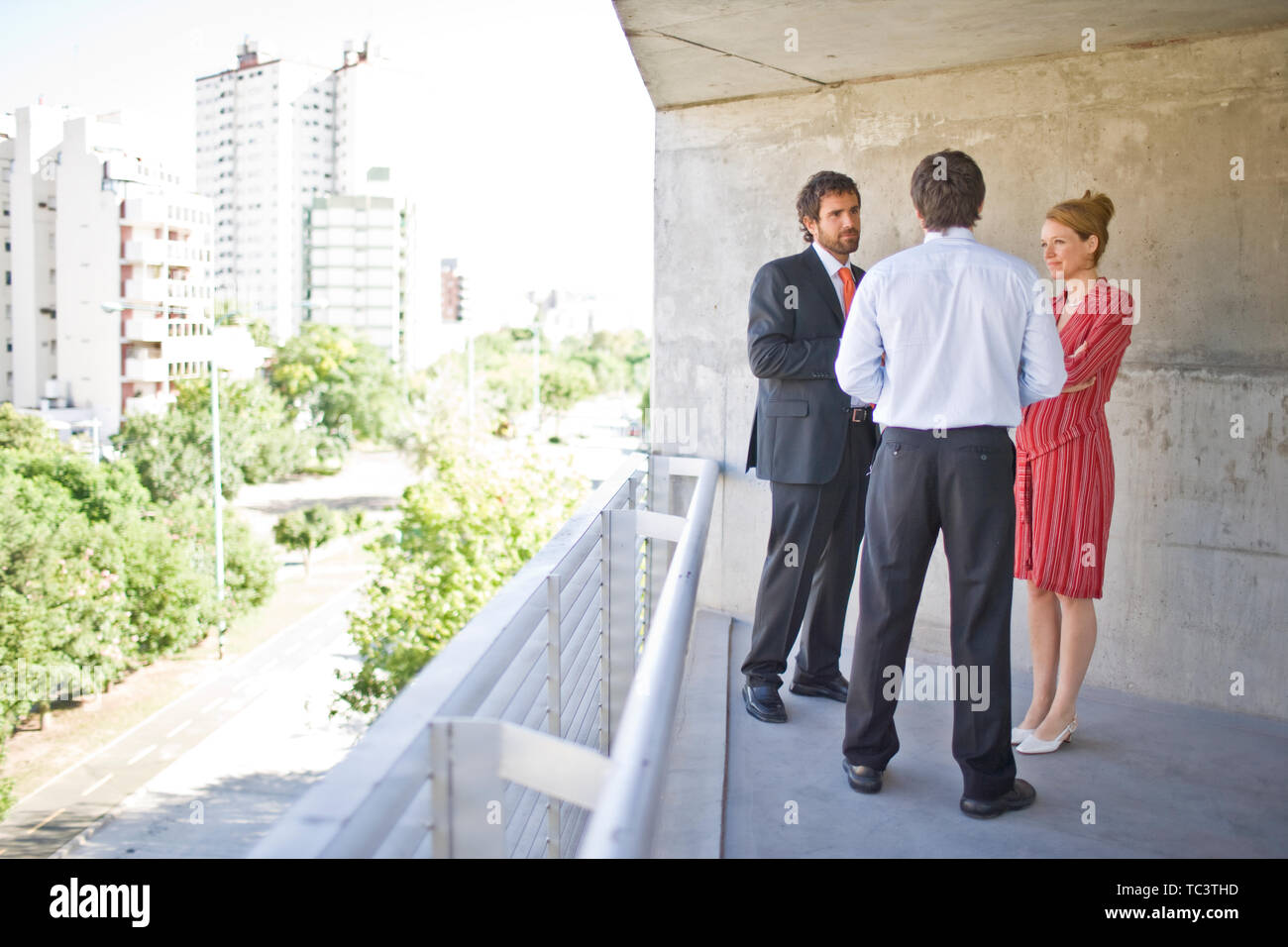 Young adult business man standing on a balcony with two colleagues ...