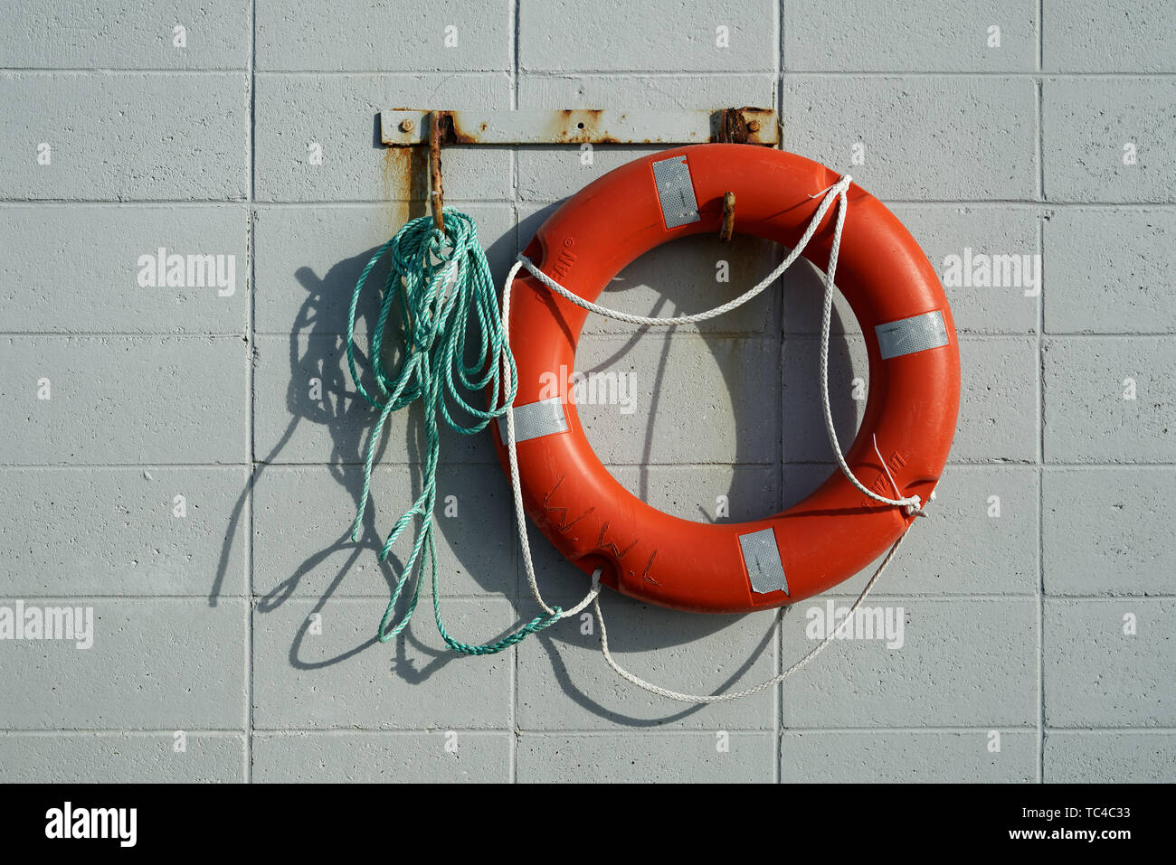 Red life saving ring attached to a tangled green rope hanging on rusty ...