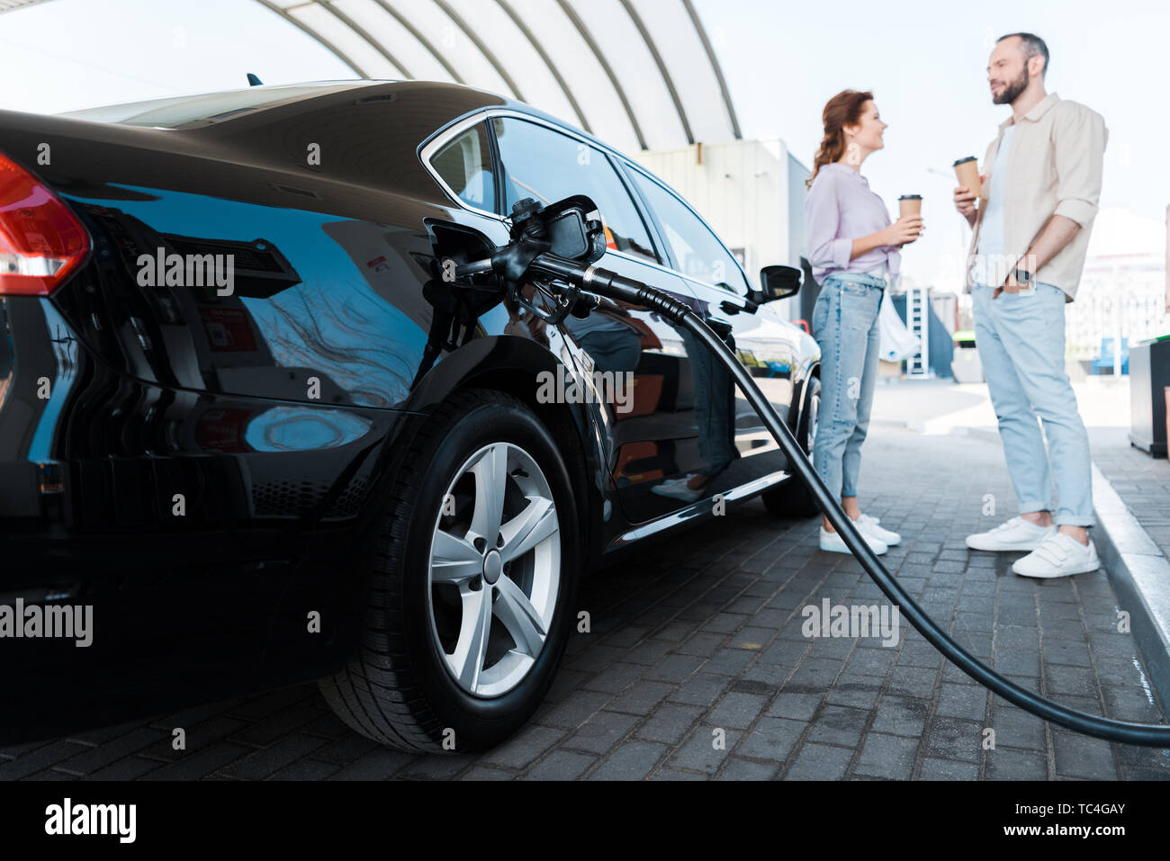 selective focus of black car refueling with benzine near man and woman ...