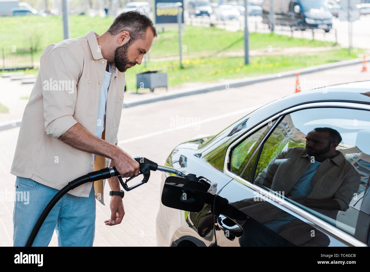 handsome man holding fuel pump and refueling black car at gas station ...