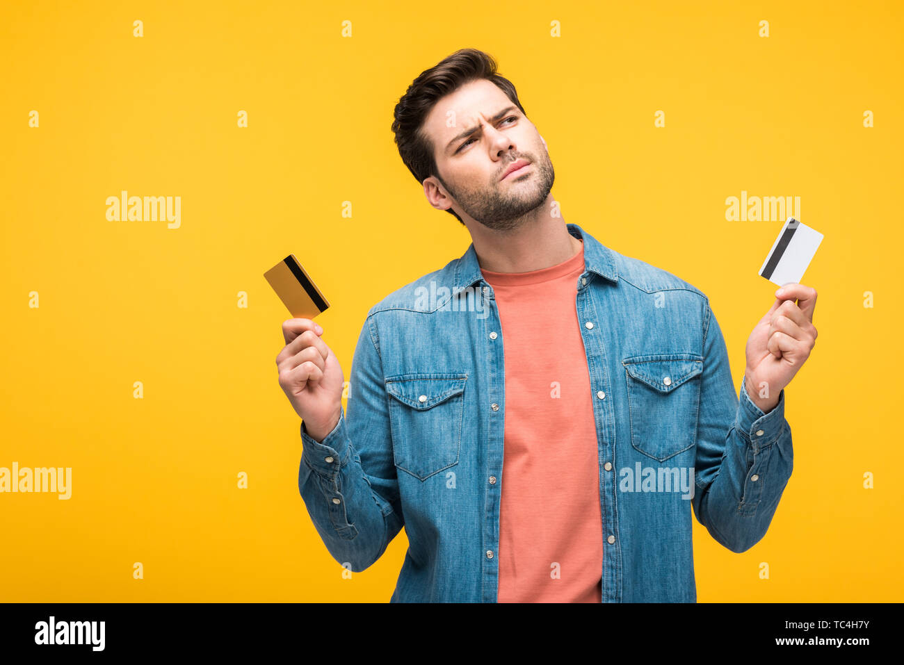 confused good-looking man holding credit cards isolated on yellow Stock ...