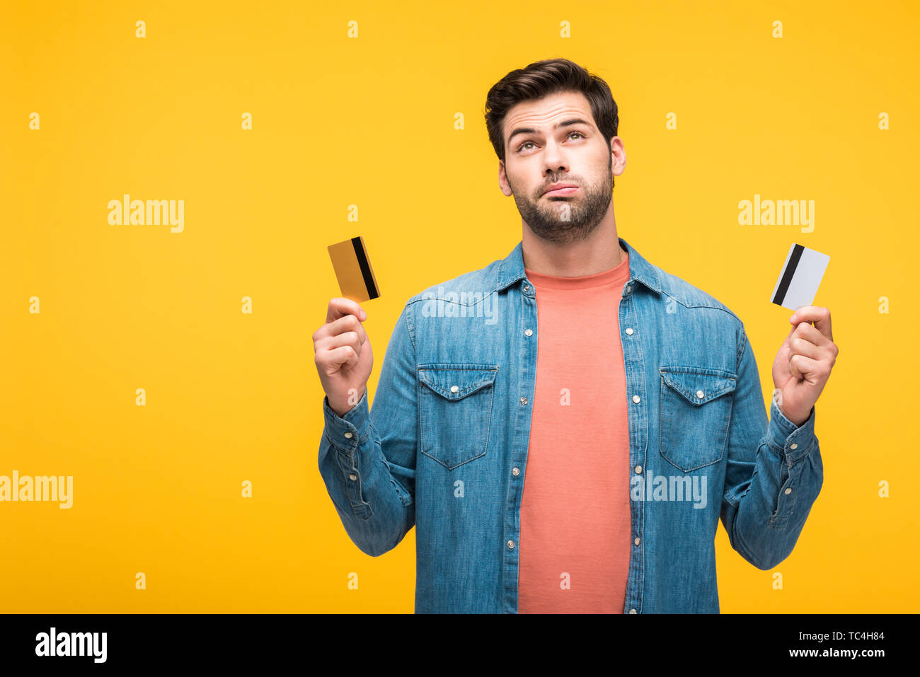 confused handsome man holding credit cards isolated on yellow Stock ...