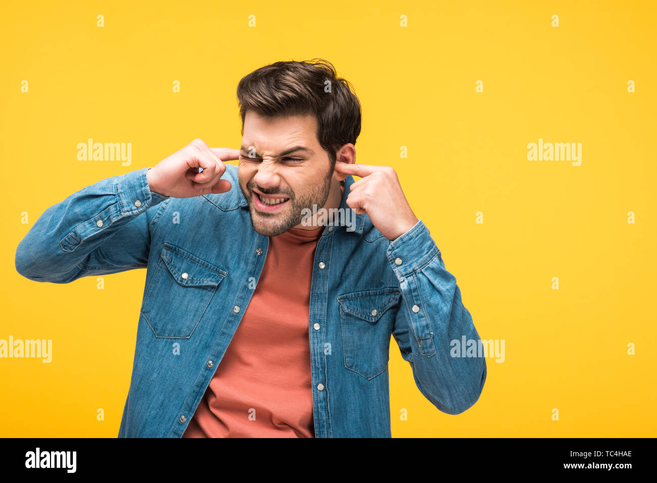 dissatisfied handsome man plugging ears with fingers Isolated On yellow ...