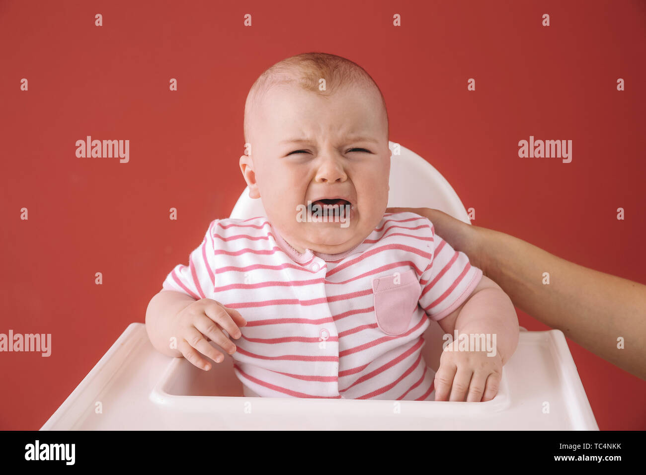 Crying little baby sitting in chair against color background Stock ...