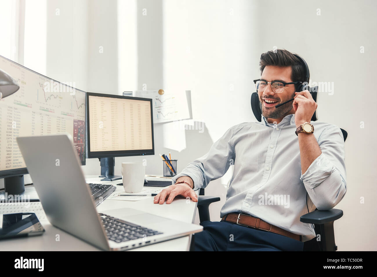 Good news. Happy young bearded trader in headset talking with client ...