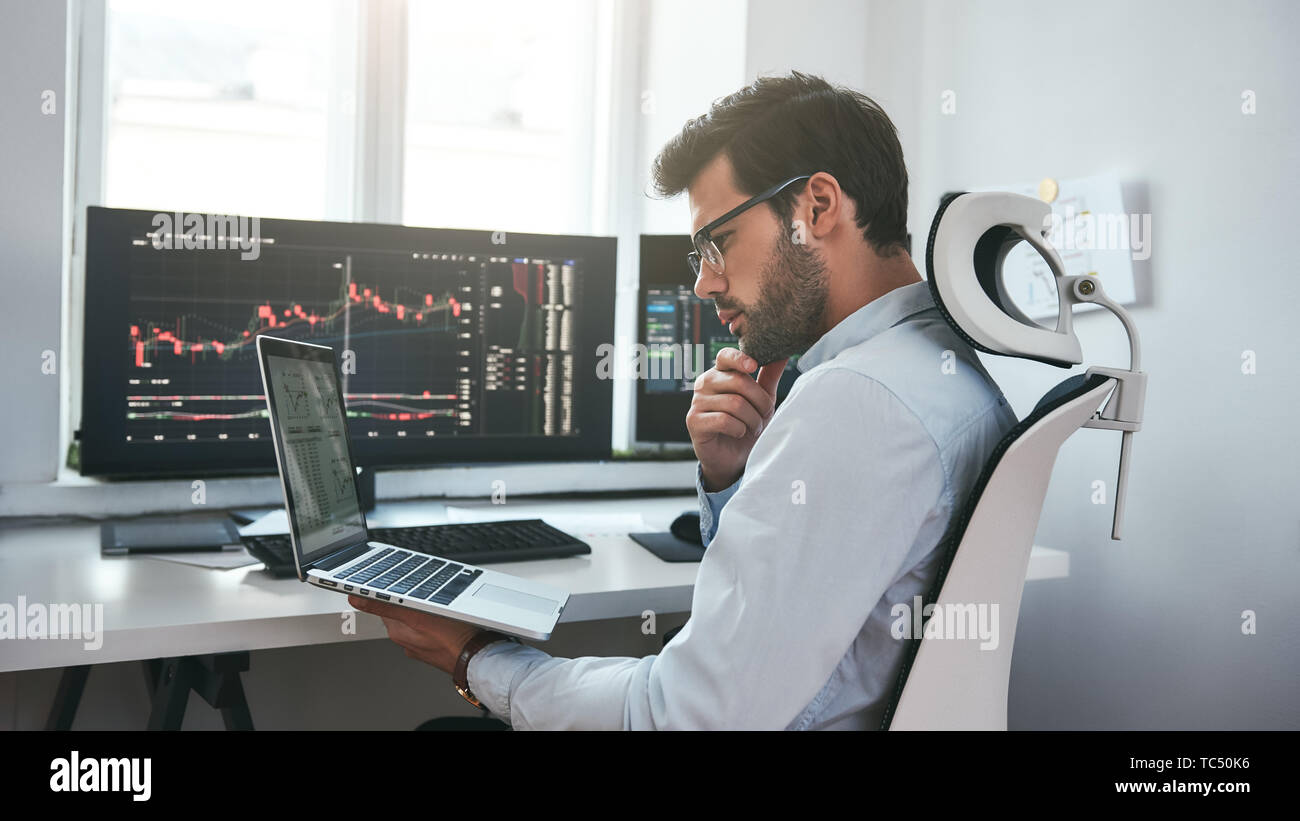 Busy day. Professional male trader wearing eyeglasses analyzing ...