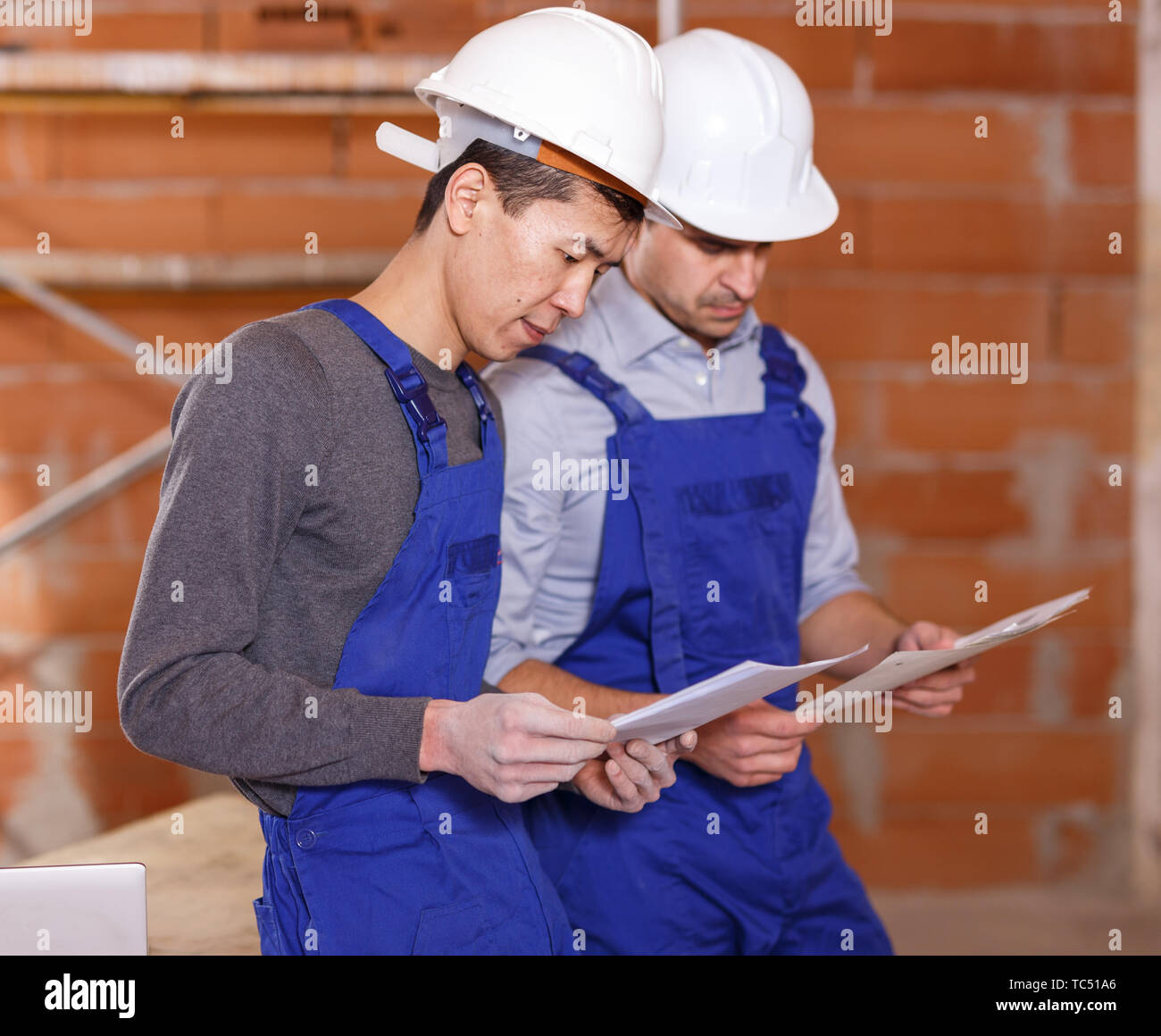 Portrait of two builders reading plan of brick building Stock Photo - Alamy