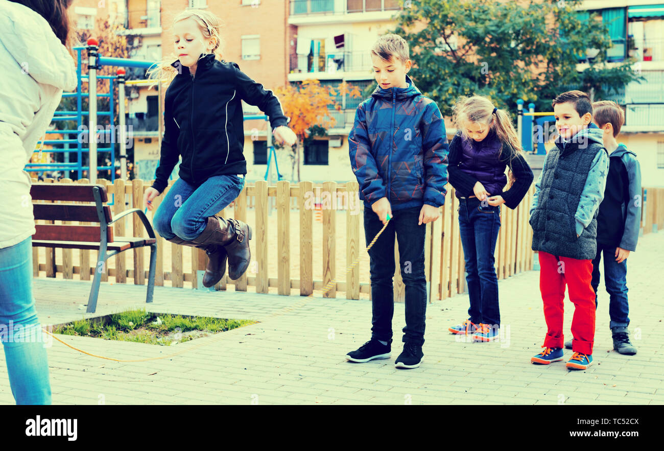 Smiling cheerful kids playing in jump rope game at city street Stock ...