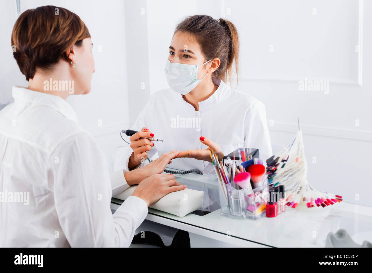 Young pleasant smiling female client doing nails in shellac technique ...