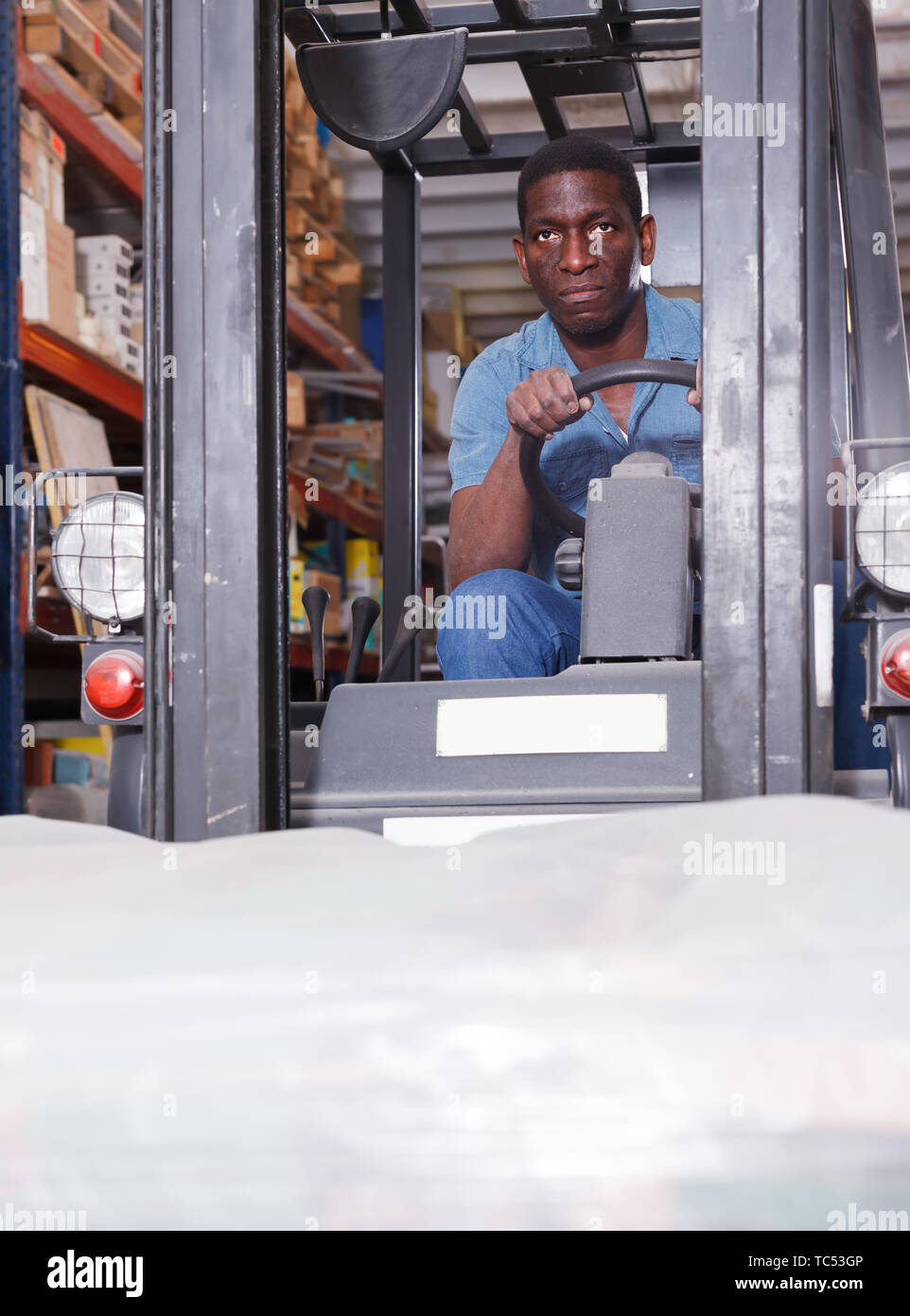 Adult African American male operator of forklift working in shop of ...
