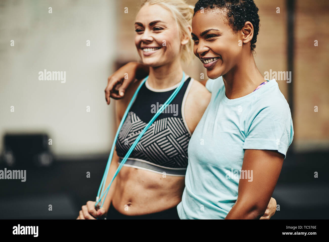 Two smiling young women in sportswear standing arm in arm together in a ...
