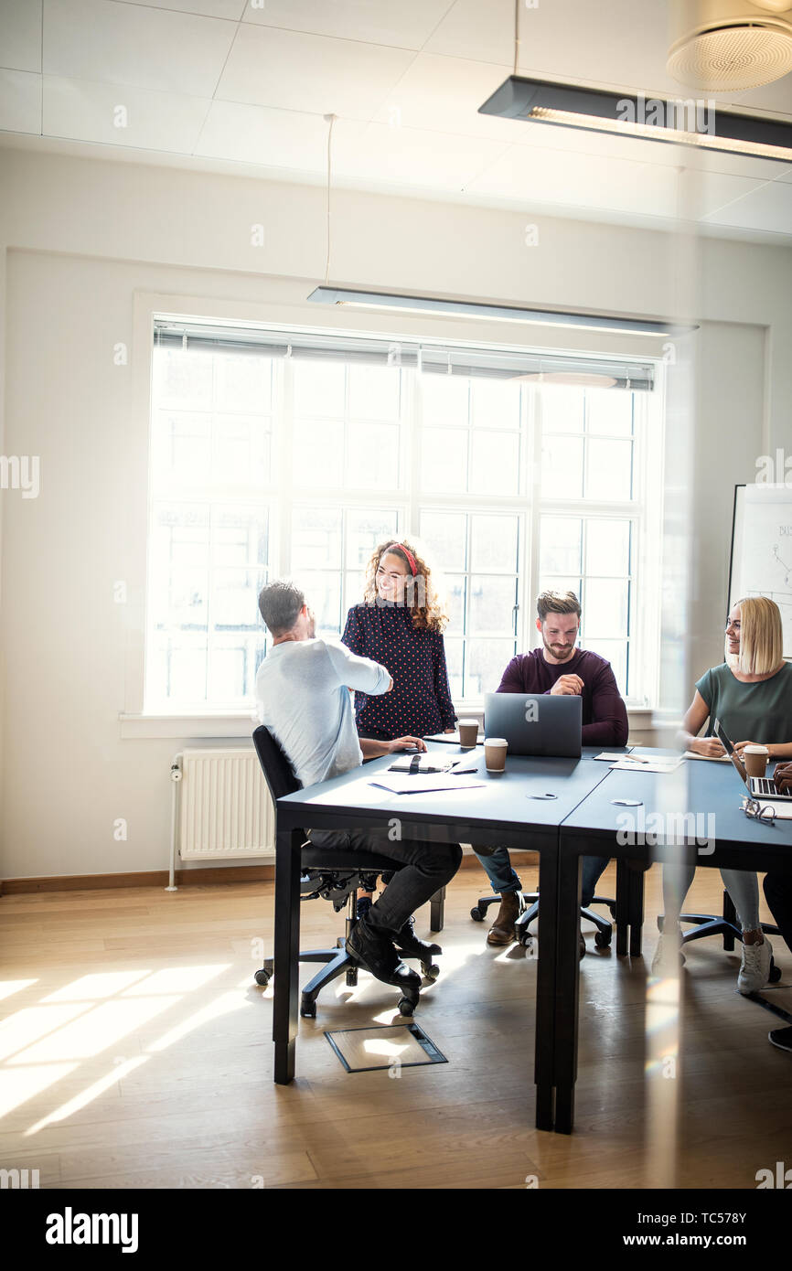 Two smiling designers shaking hands while working around a boardroom ...