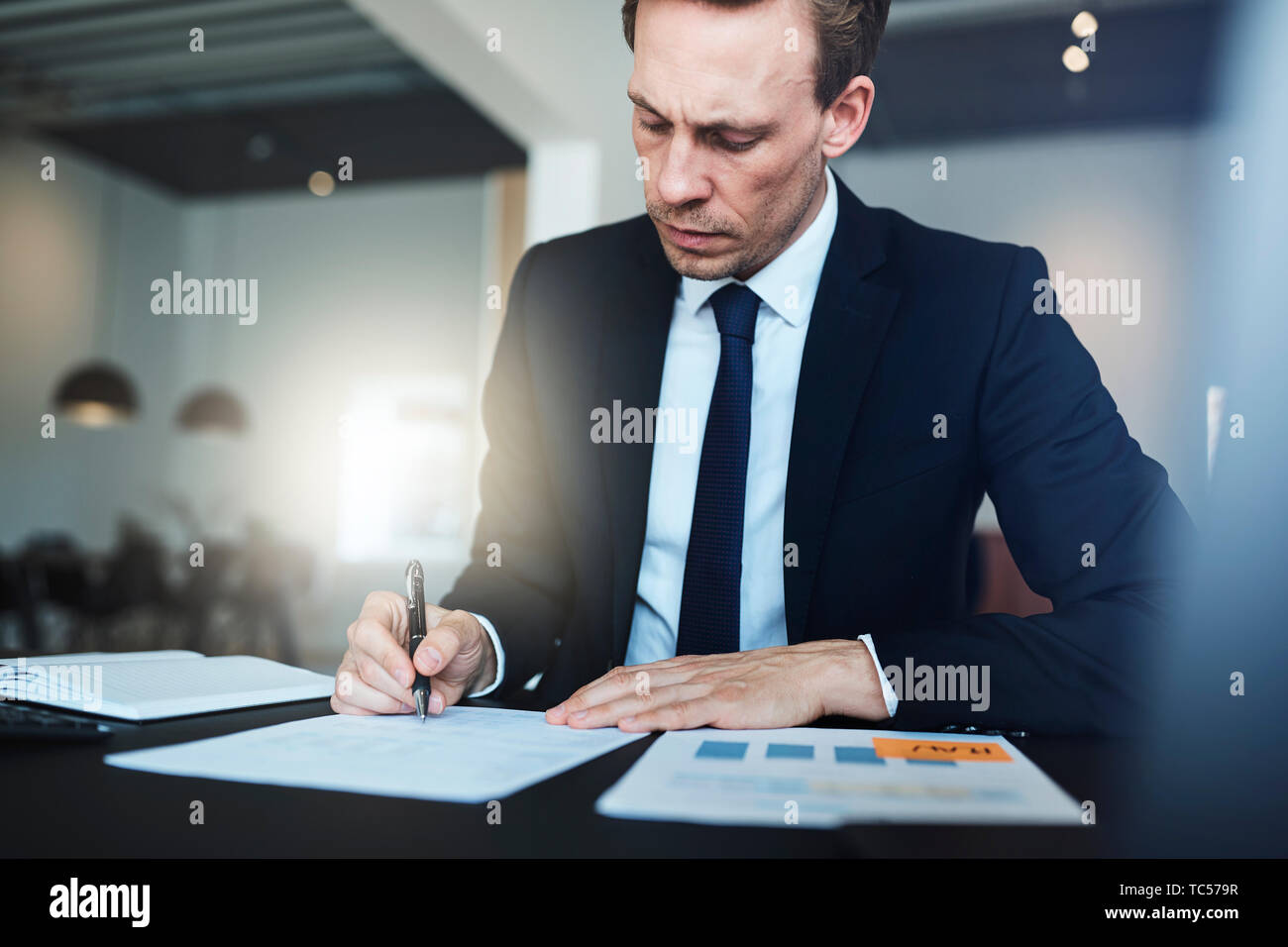Businessman signing documents while going over paperwork at his desk in ...