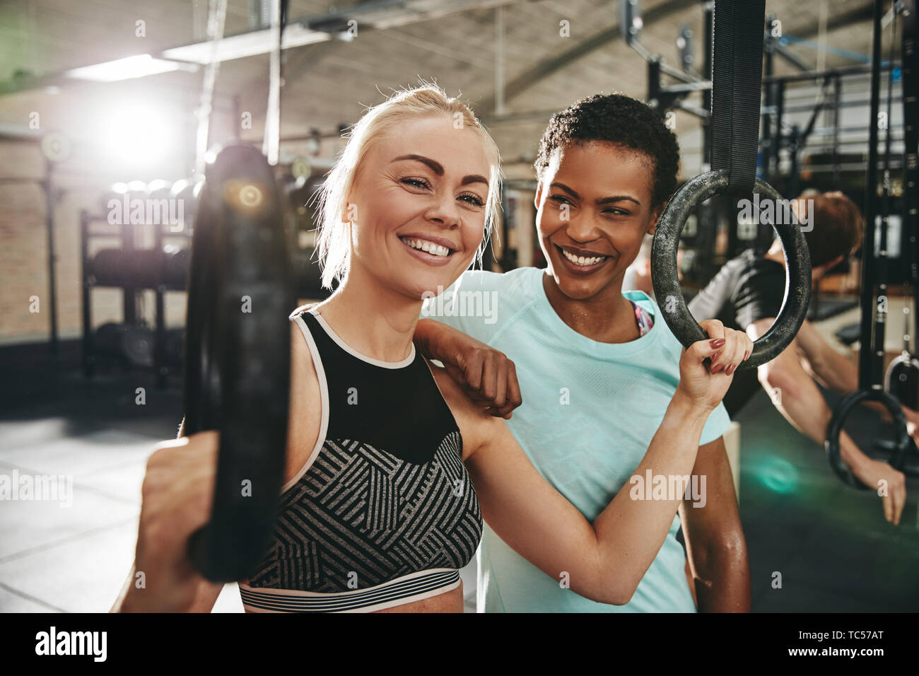 Two smiling young female friends in sportswear standing by rings in a ...
