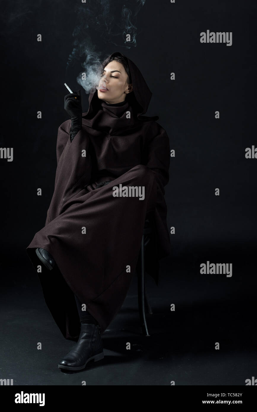 pensive woman in death costume sitting on chair and smoking cigarette ...