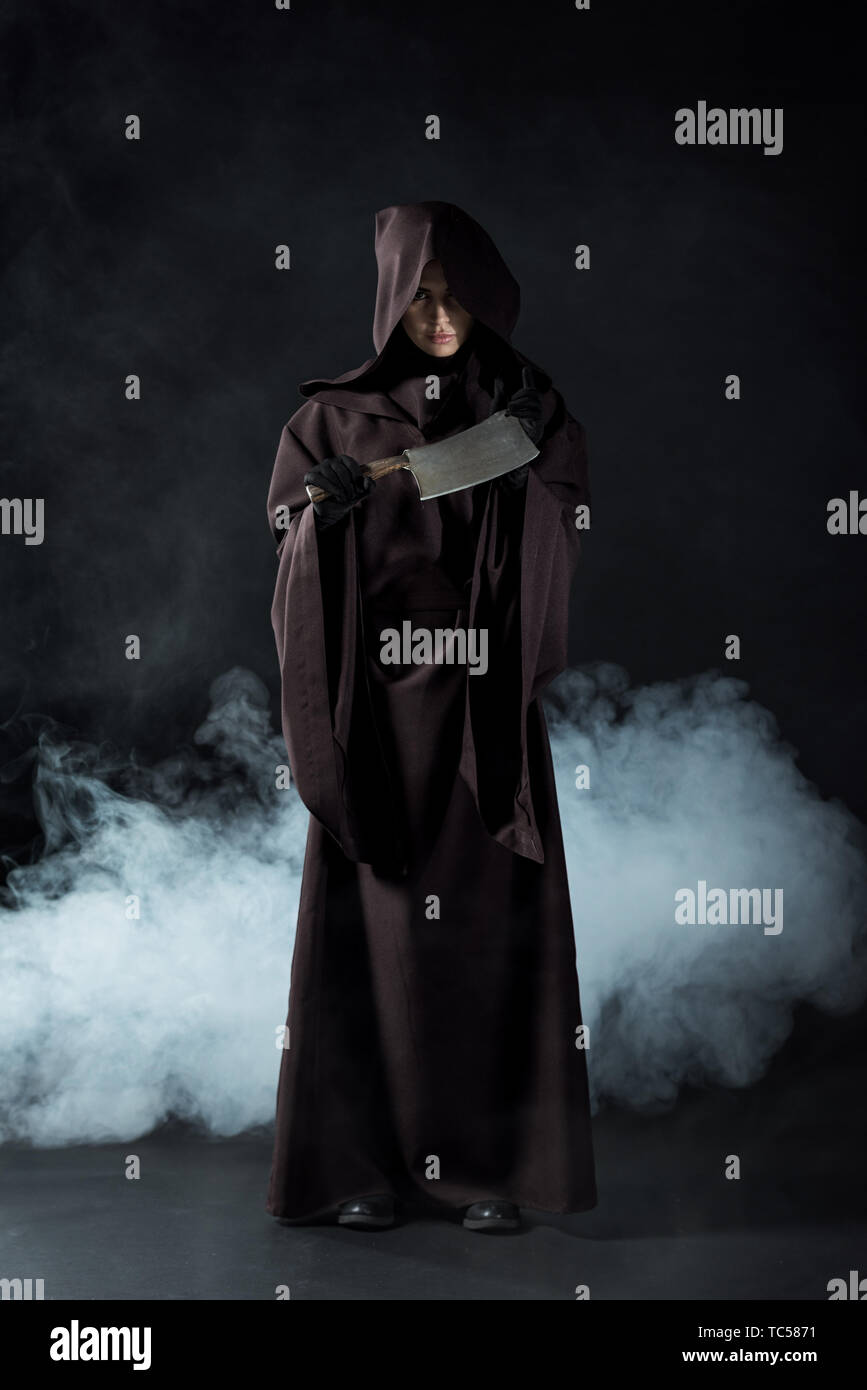 full length view of woman in death costume holding cleaver in smoke on ...