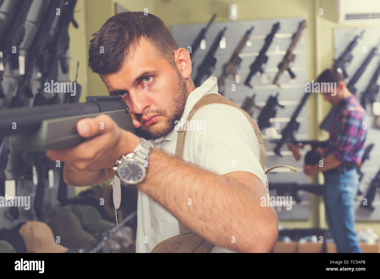 Portrait of adult man which is choosing air-powered gun in army market ...