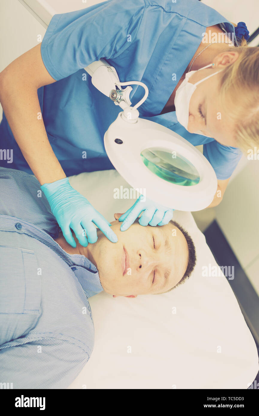 Woman specialist is cleaning skin of patient with using magnification ...