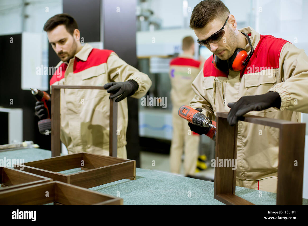 Two handsome young workers assembling furniture in the factory Stock ...