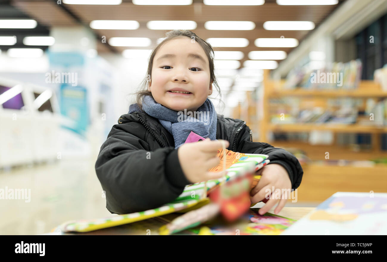 Little Asian girl reading in the library Stock Photo - Alamy