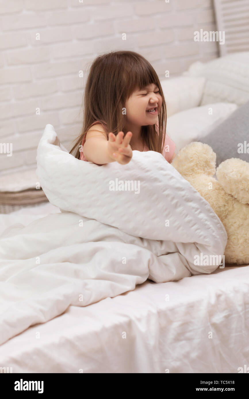 cute little child girl wakes up from sleep in bed. child shows gesture ...
