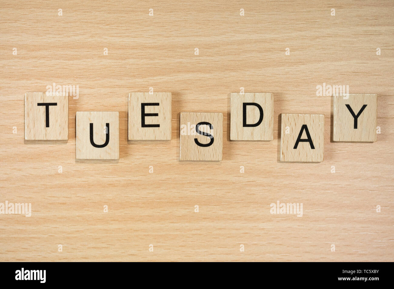 The word Tuesday, spelt out using wooden tiles on a wood effect ...