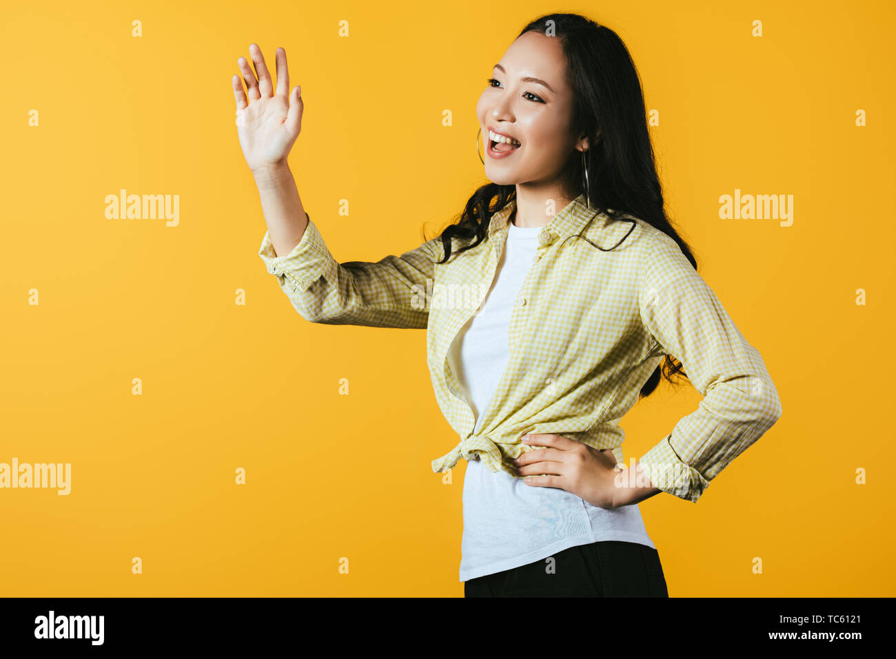 brunette asian girl waving isolated on yellow Stock Photo - Alamy