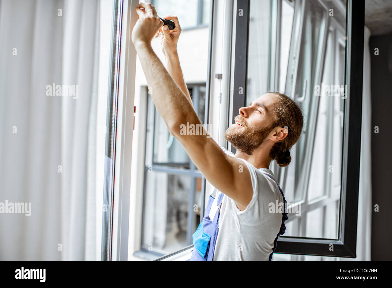 Workman in overalls installing or adjusting plastic windows in the ...